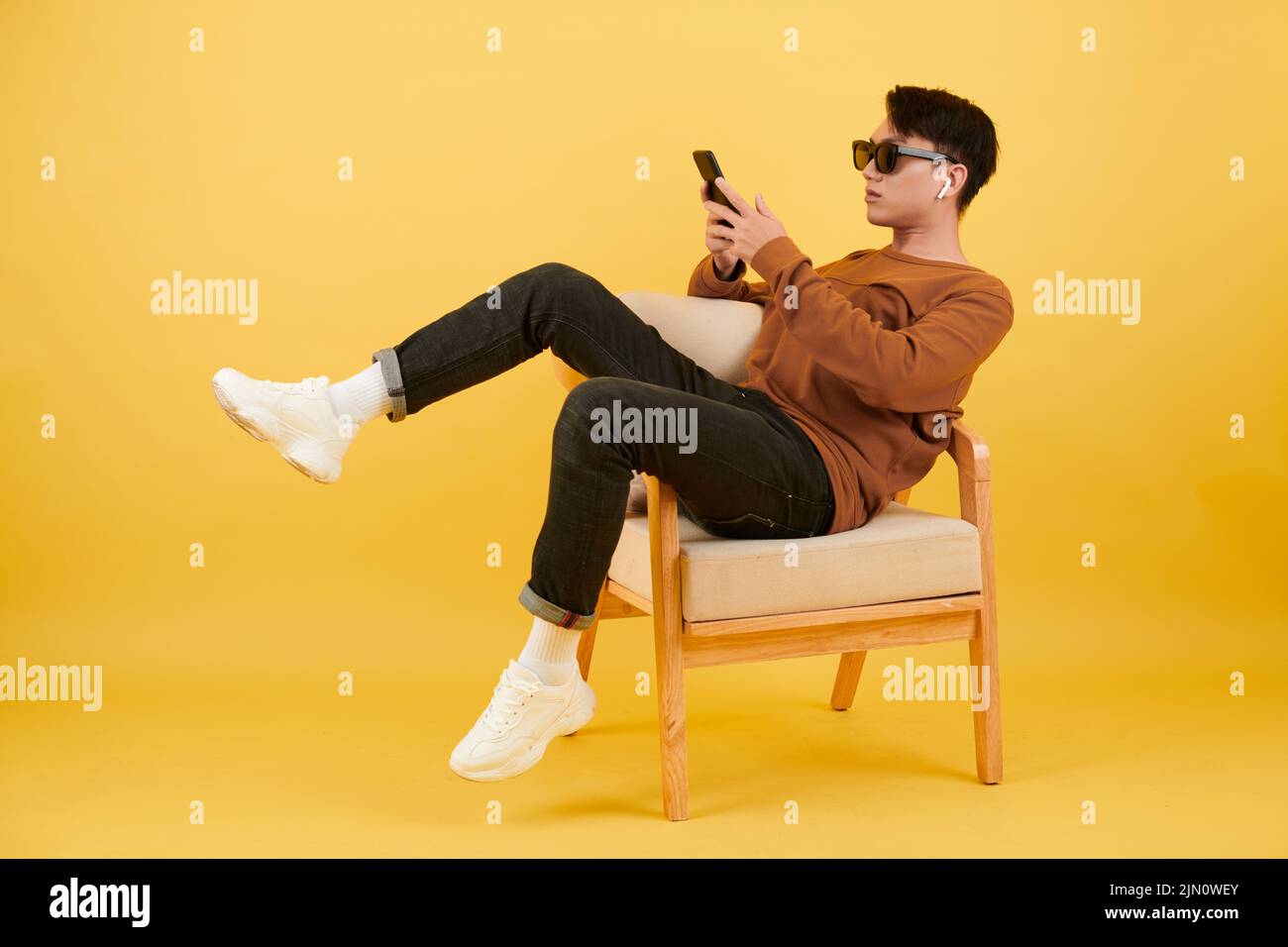 Serious young man sitting on armchair and texting friends Stock Photo ...