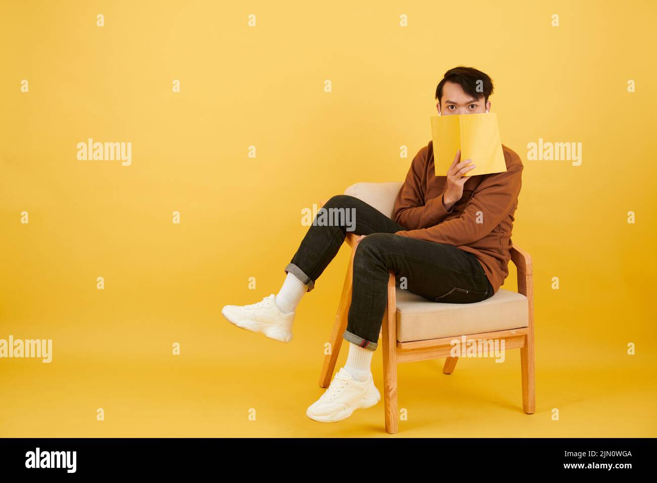 Serious young man covering half face with opened book and looking at ...