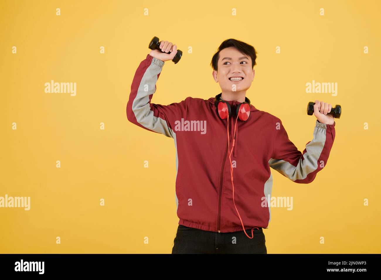 Smiling young man in windbreaker working out with dumbbells Stock Photo ...