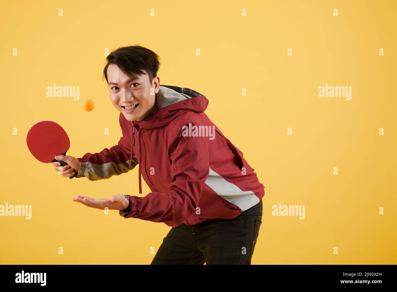 Smiling young Asian man playing table tennis, isolated on yellow Stock ...