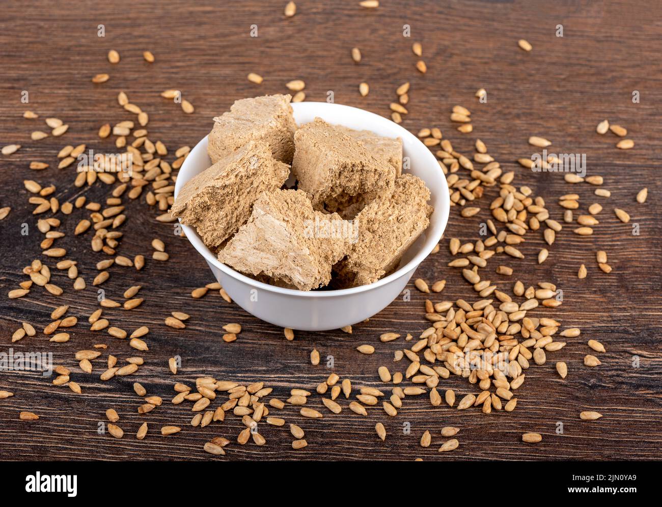 Sunflower halva chopped into pieces in a white porcelain bowl with sunflower seeds around the ...