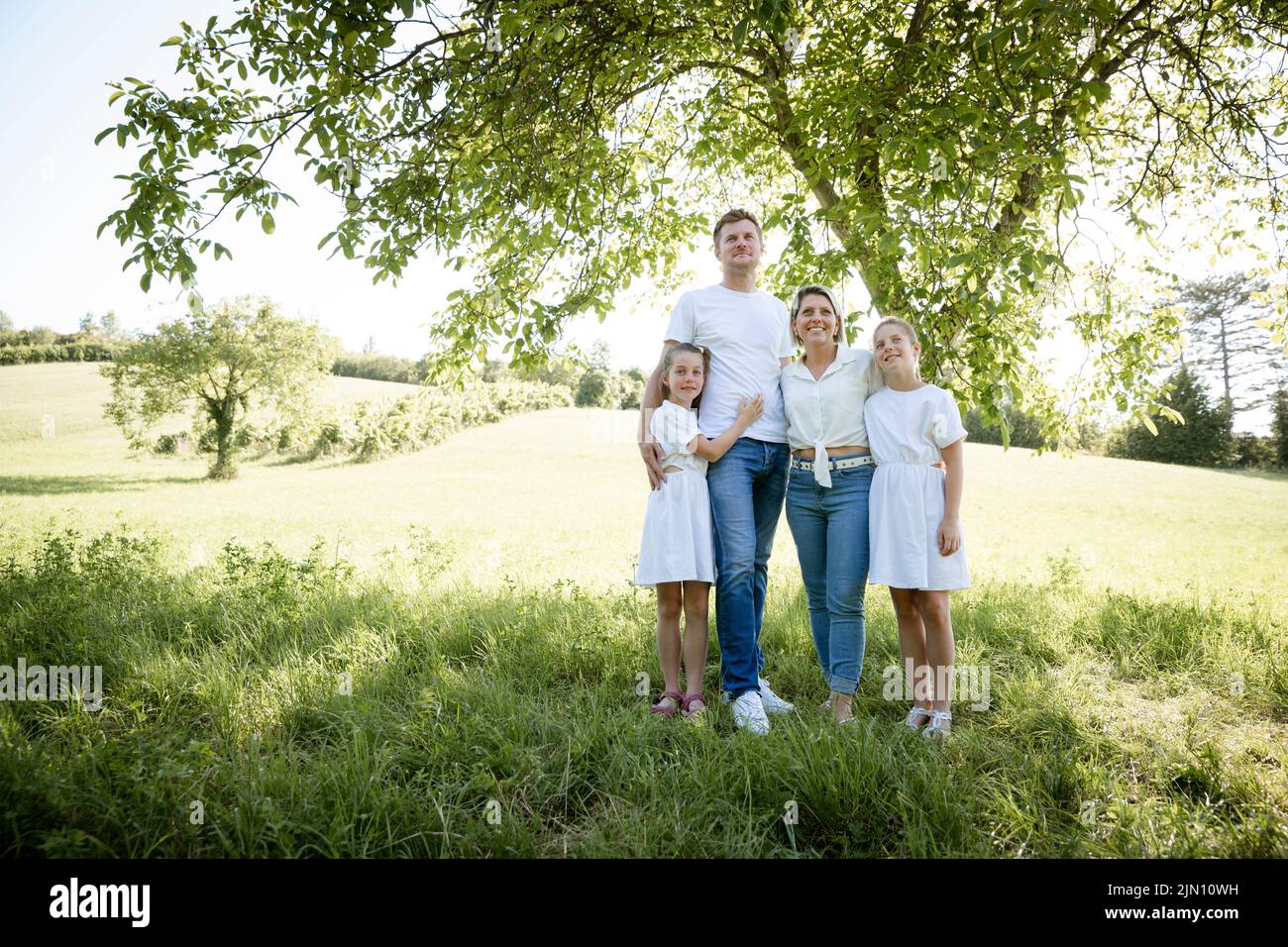 beautiful family with two girls is standing in meadow near walnut tree ...