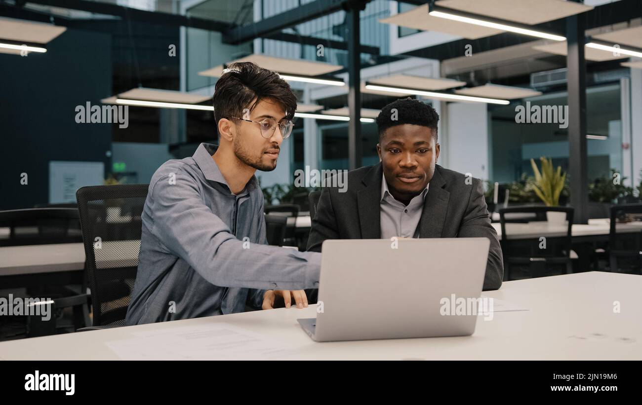 Two multicultural professional male co-workers men colleagues sit at ...