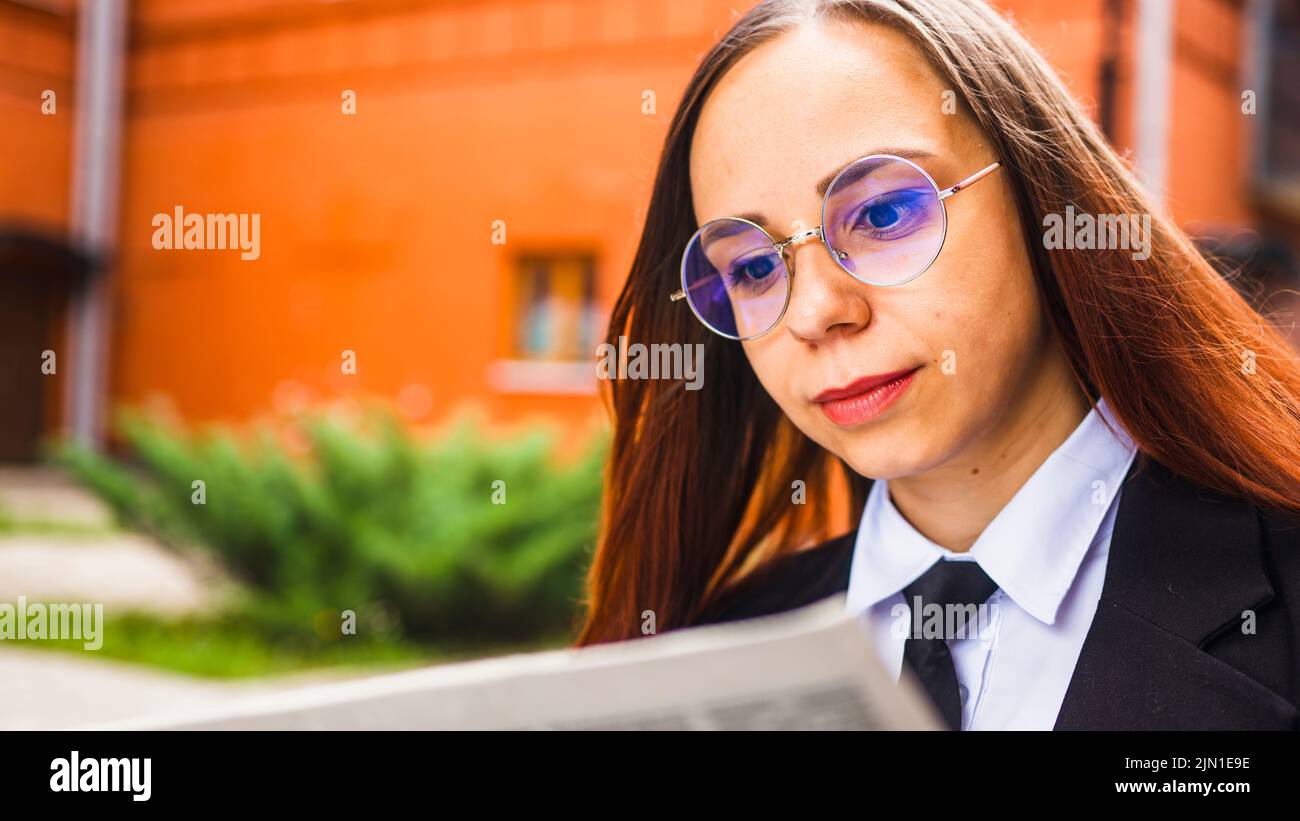 Thoughtful young woman reading newspaper on street. Confused young ...