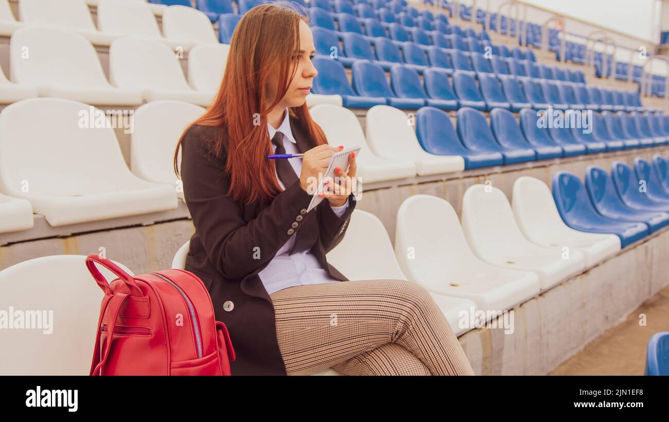 Young woman with notepad, pen sitting on stadium bleachers alone ...