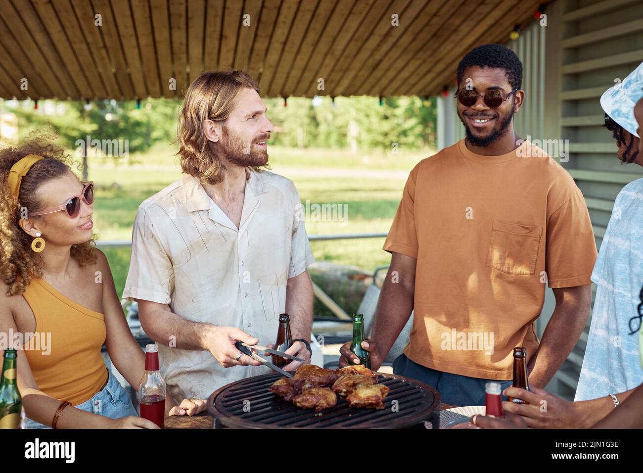 Portrait of two young men grilling meat outdoors with diverse group of ...