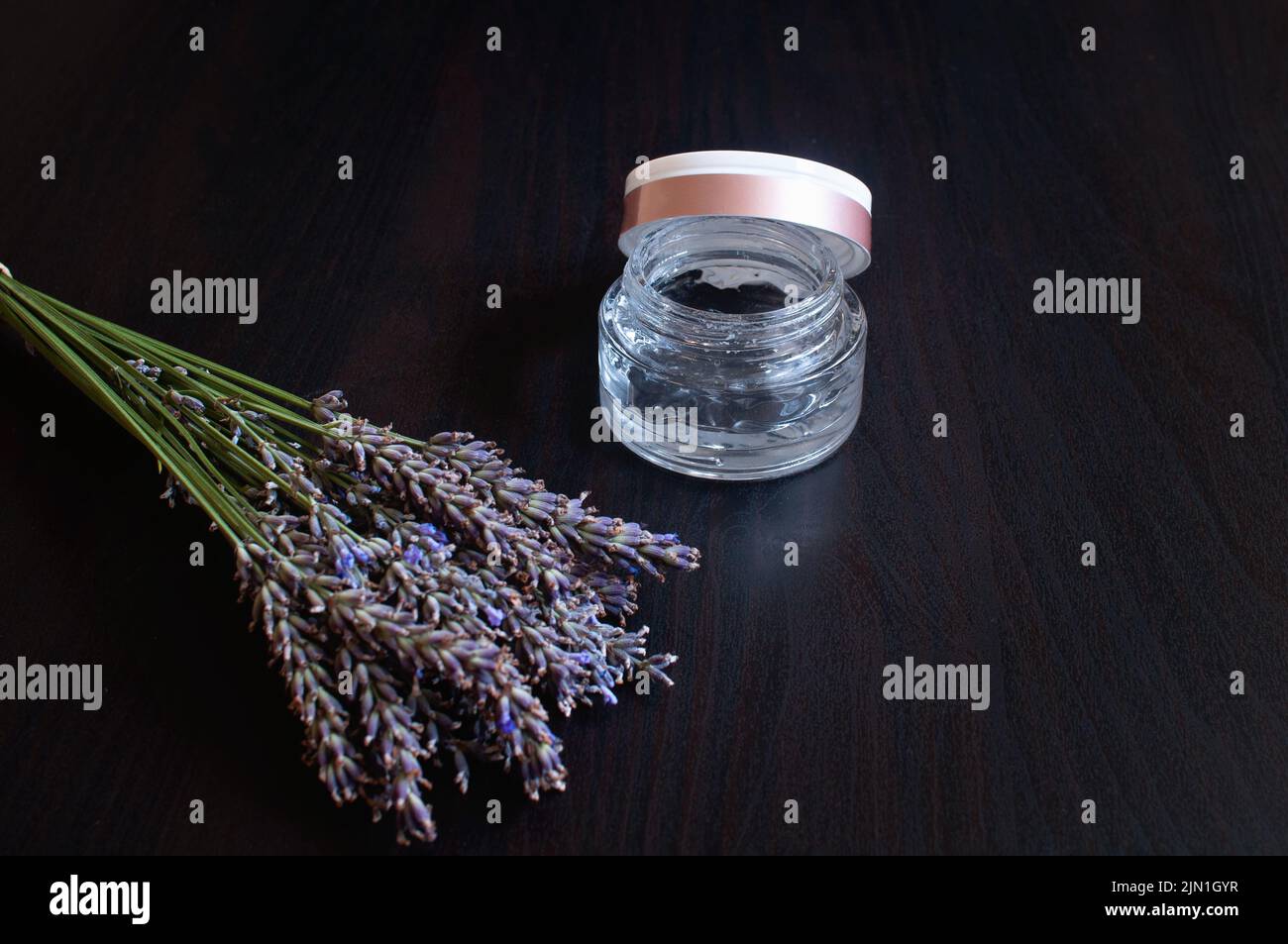 glass jar with transparent gel and fresh lavender flowers on a black ...