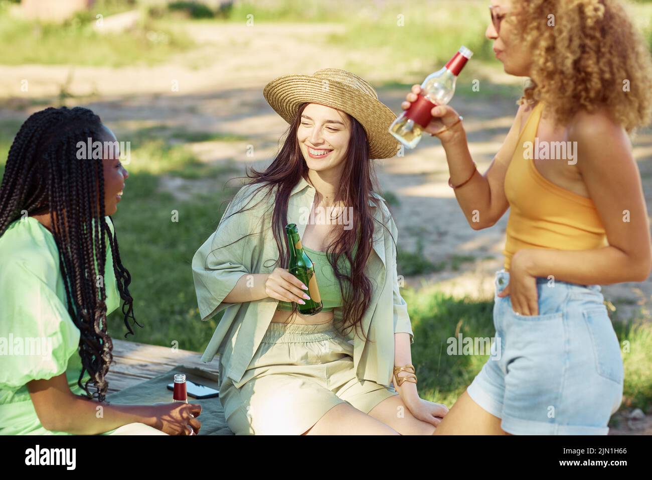 Diverse group of smiling girls drinking beer outdoors in sunlight and ...