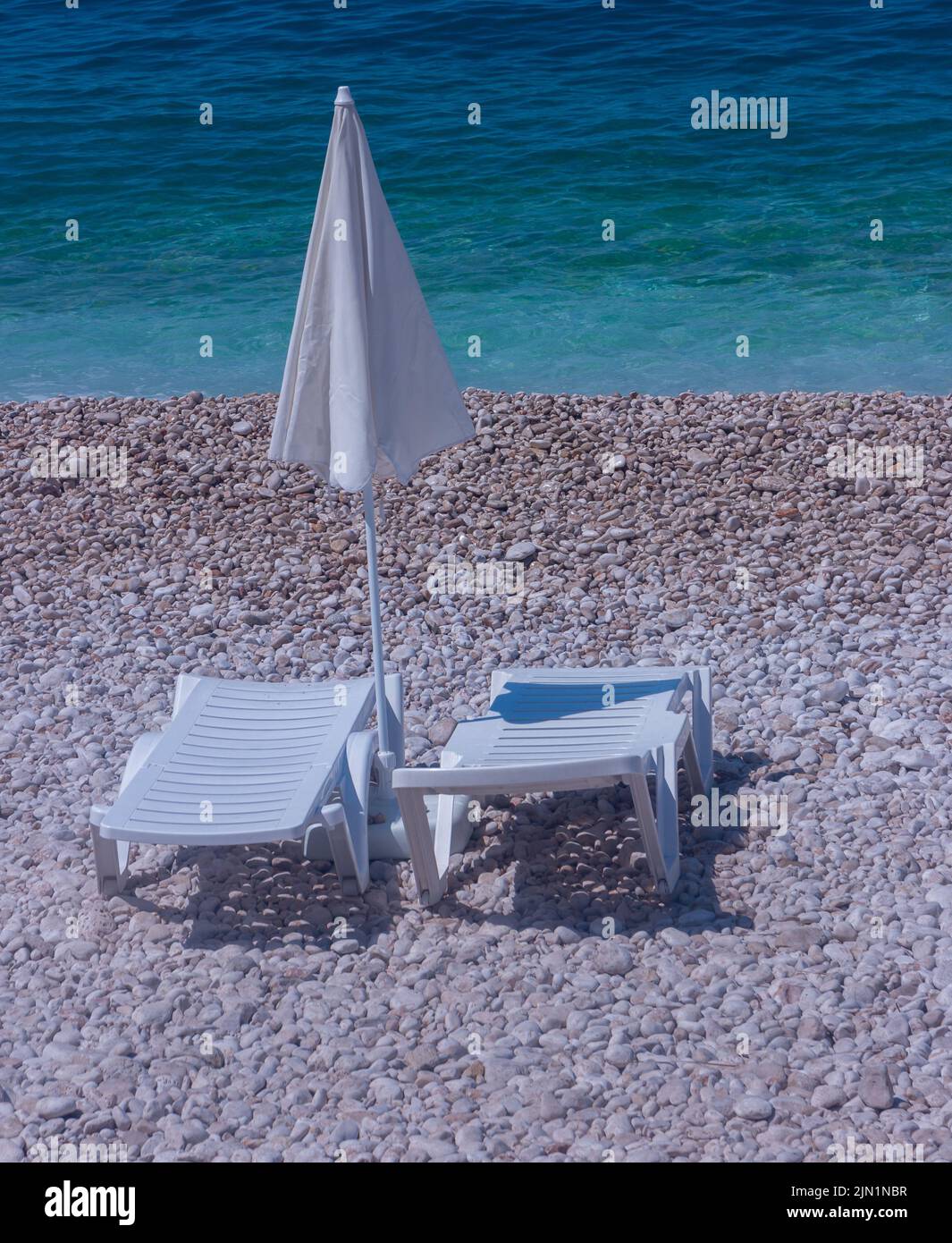 Sunbeds and an umbrella on a beach, white sunbeds, an umbrella, and ...