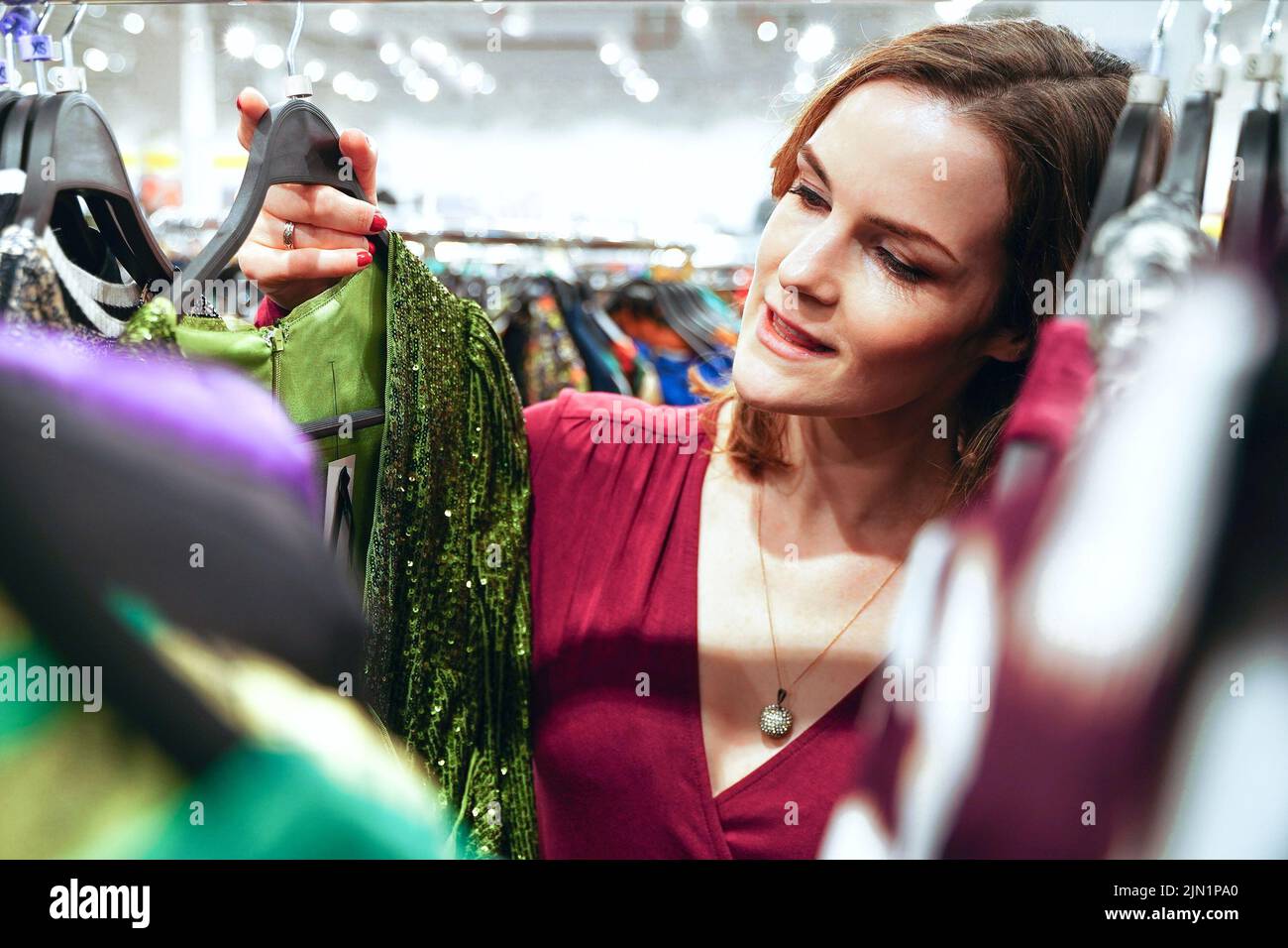 Pretty woman chooses clothes in store. Girl buyer looks curiously at ...