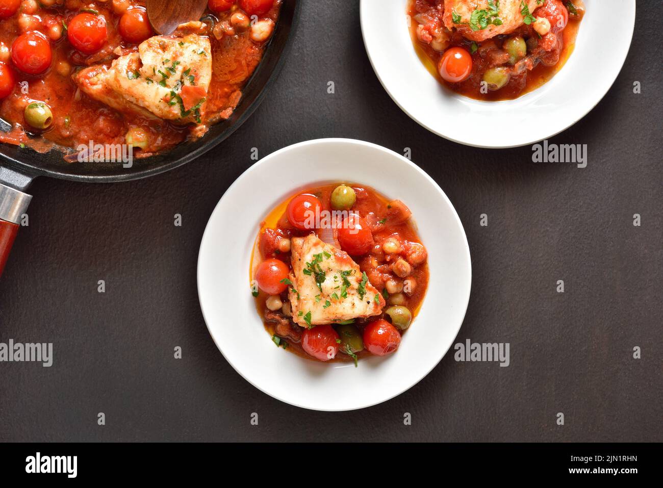Cod stew with chickpeas, cherry tomatoes and olives over dark stone ...