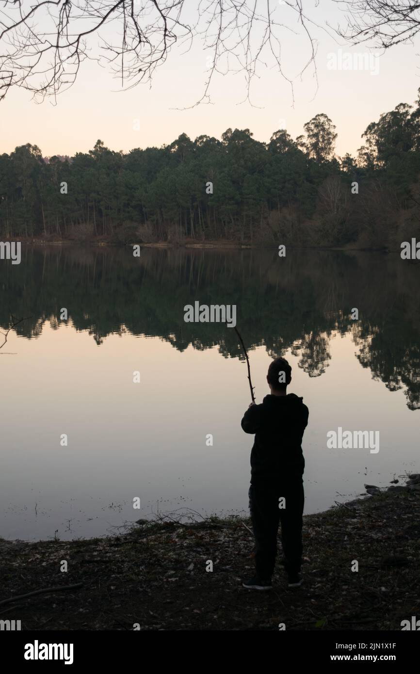 man fishing with a tree branch in a lake in the forest at dusk Stock ...