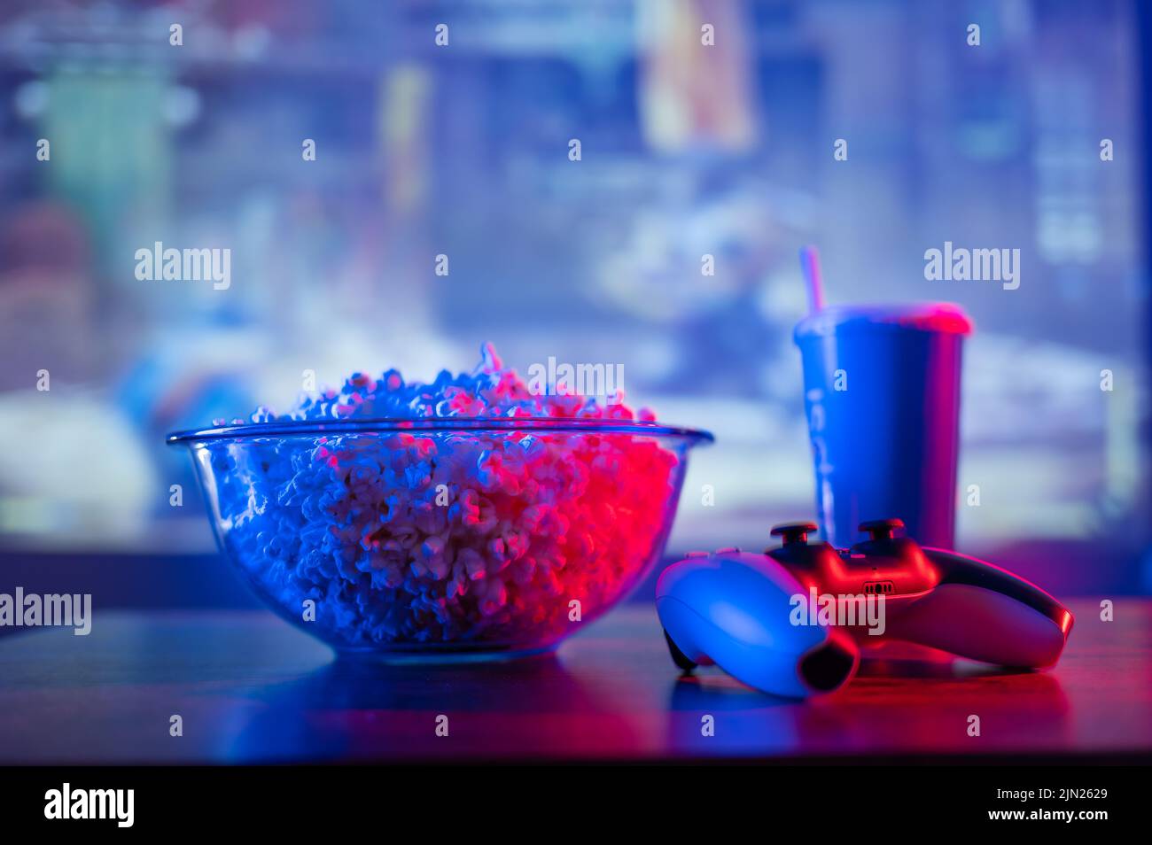 On the table is a glass bowl of popcorn, a drink in a plastic cup, and ...