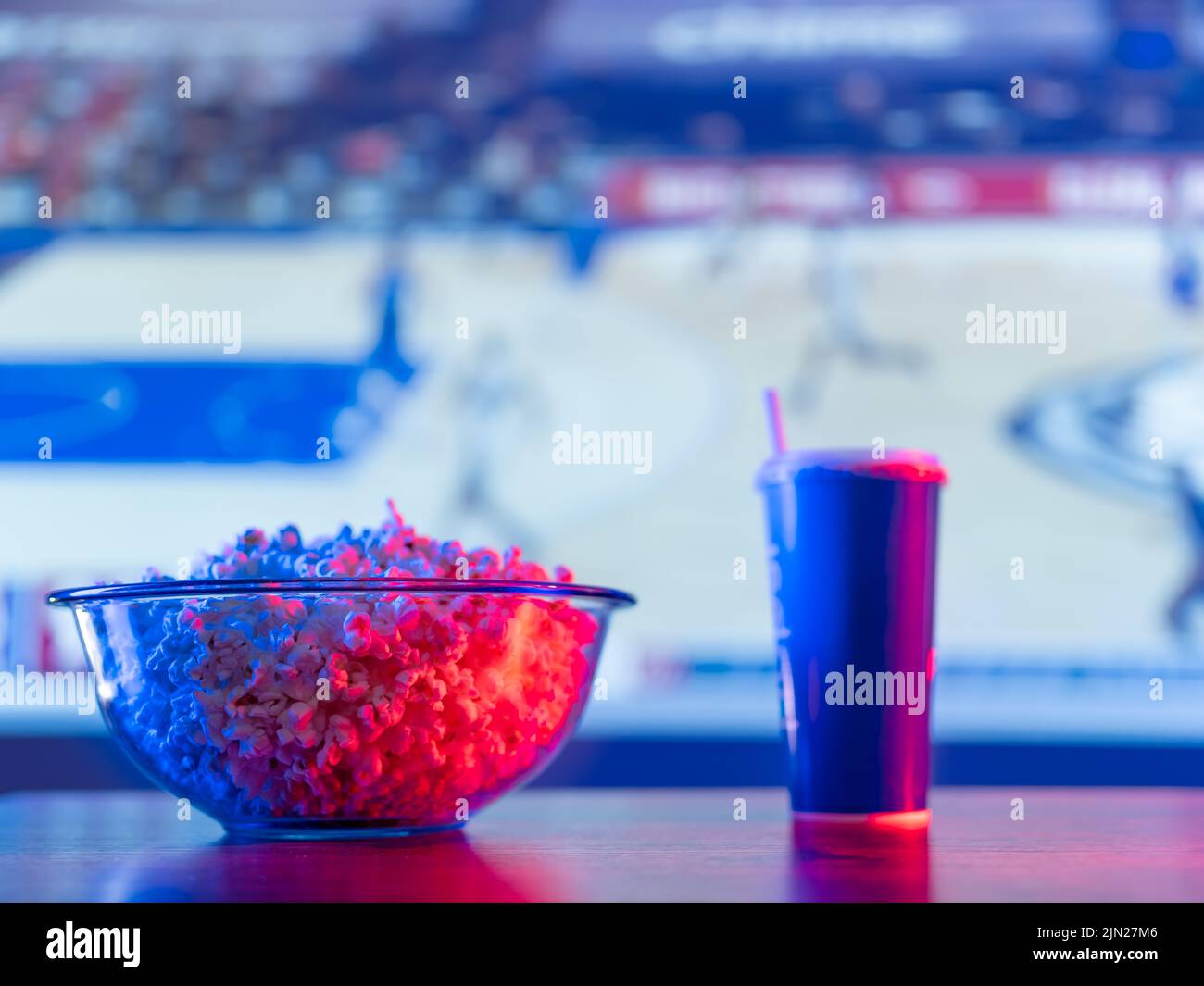 A sports match on the screen of a large plasma TV. Popcorn in a glass ...