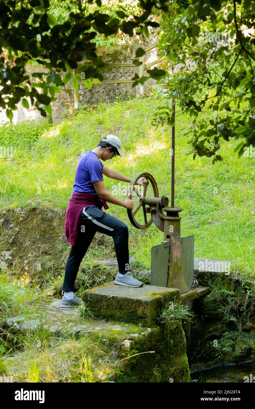 young man turning a wheel to close the dam for irrigation of the creek ...