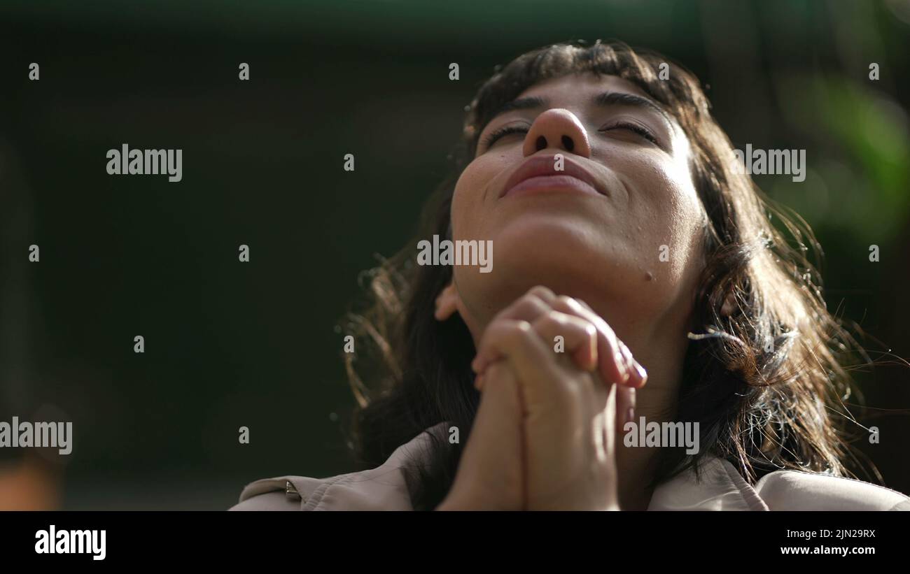Hopeful woman praying to God standing outside looking at sky. Girl closing eyes in meditation ...