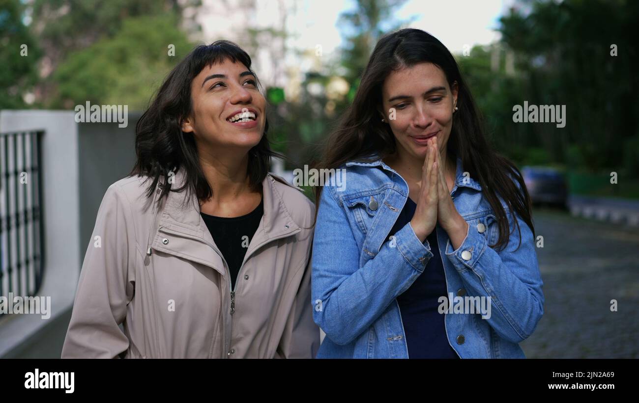 Two happy young women girlfriends walking outside laughing and smiling ...