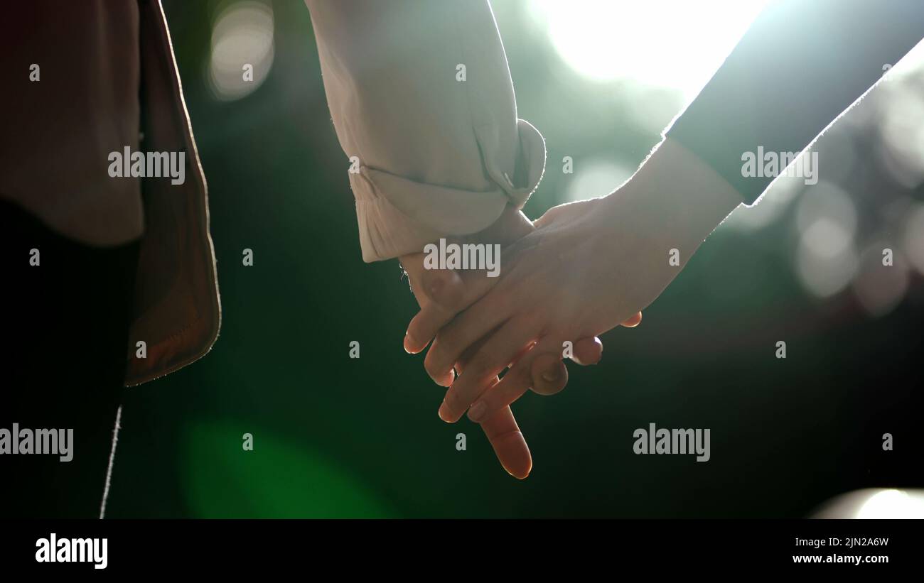Two people joining hands outside with sun flare in background. Closeup ...