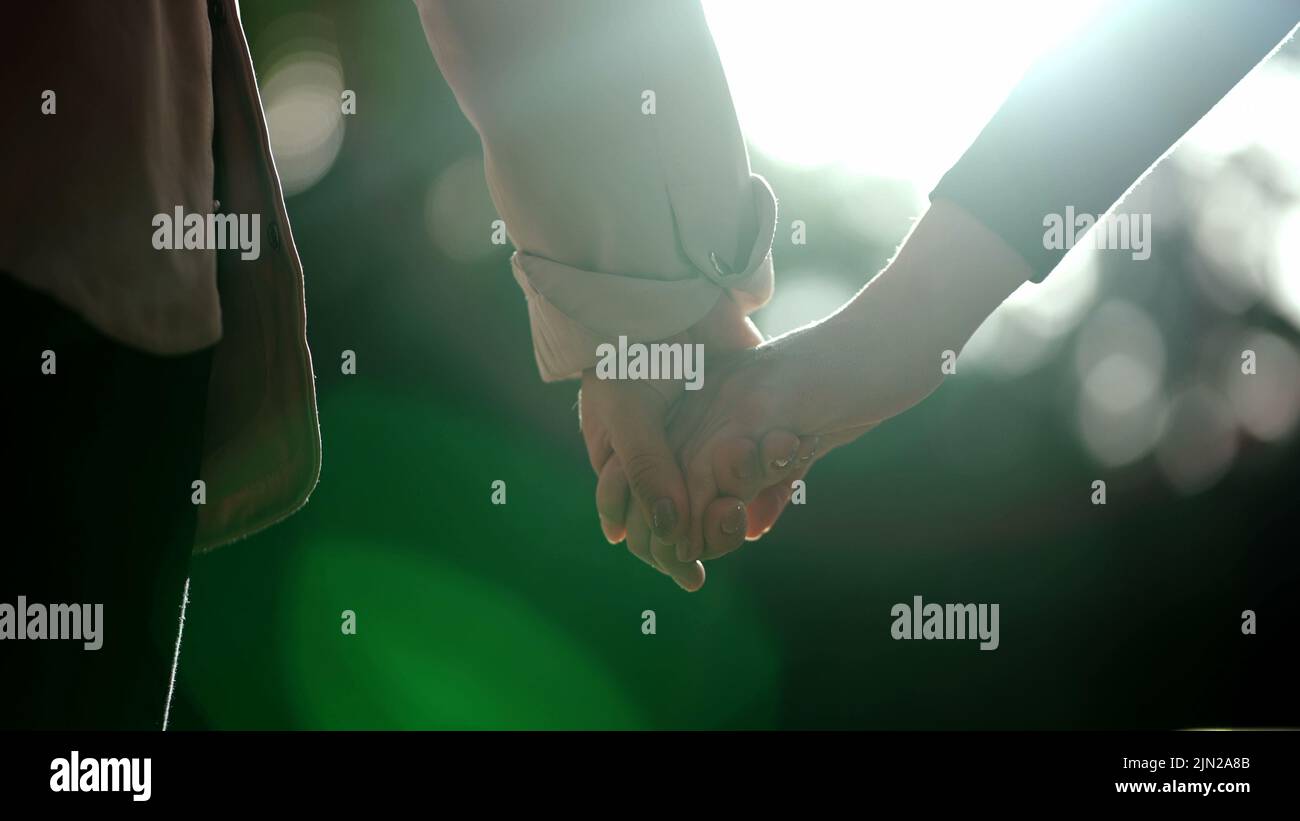 Two people joining hands outside with sun flare in background. Closeup ...