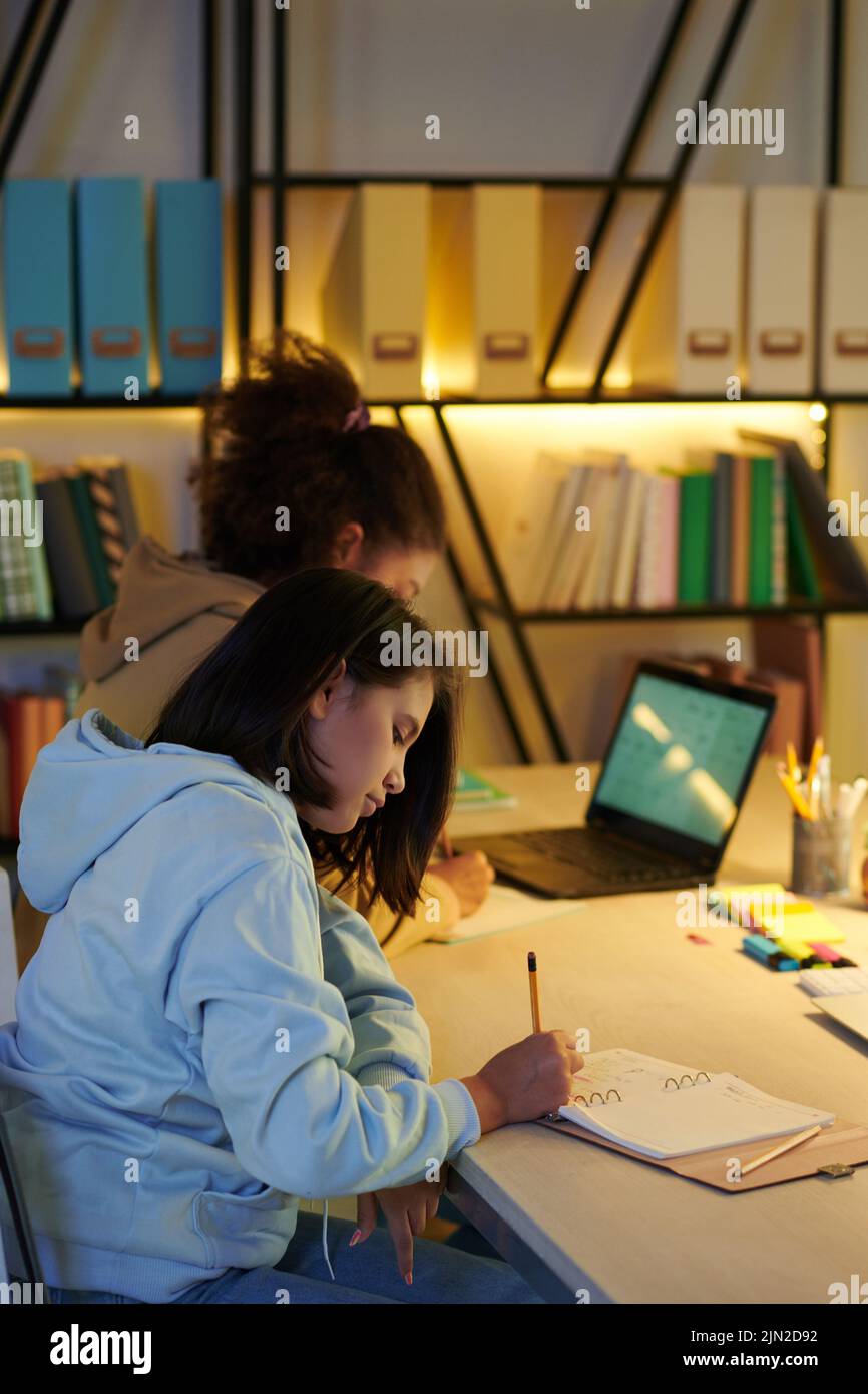 Friends studying in school library, writing and sketching in textbooks ...