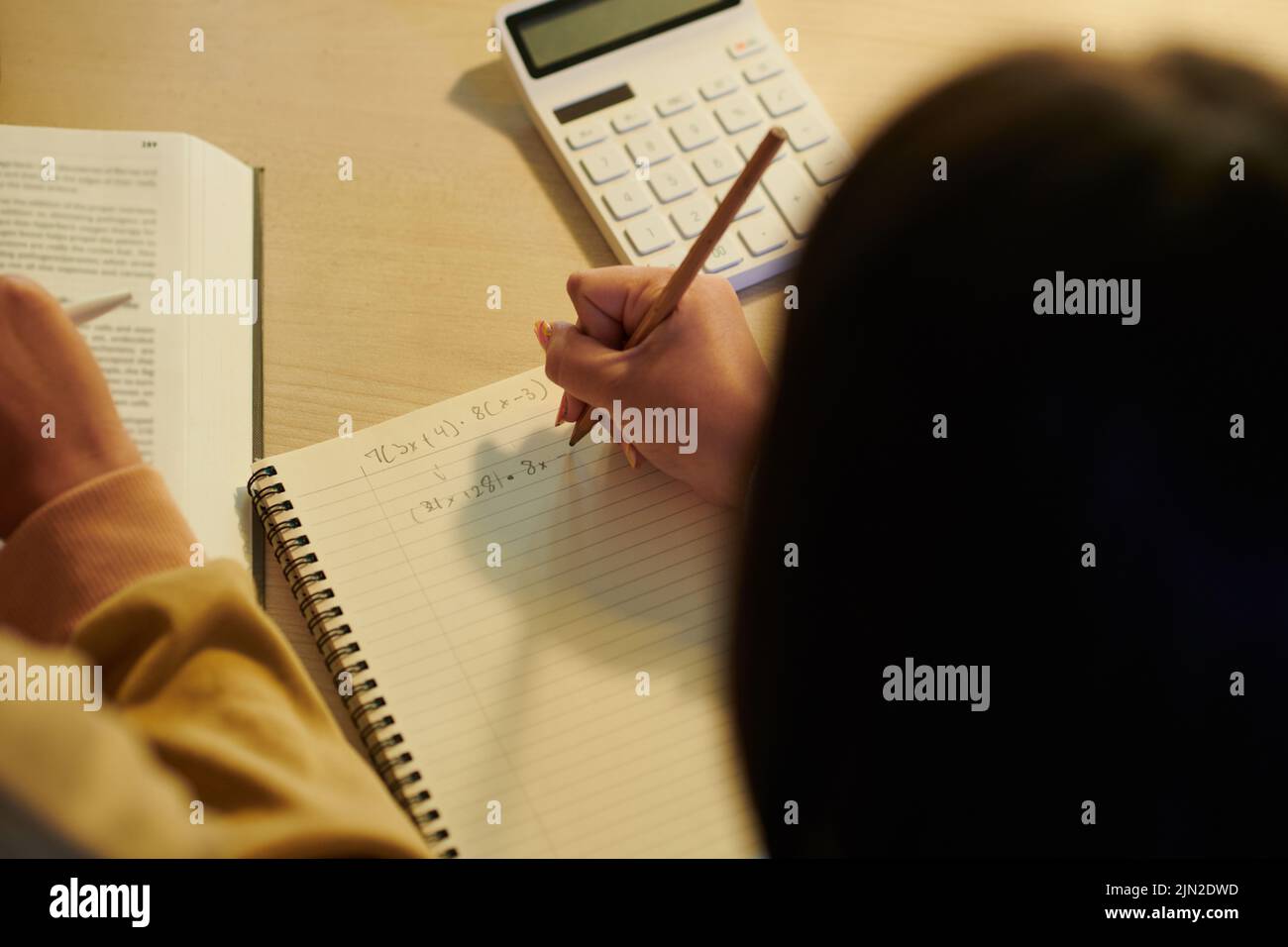 Schoolgirl solving equations and writing in textbook, view over ...