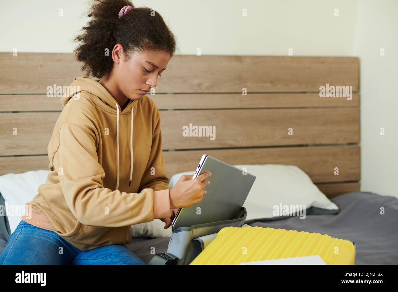 Serious teenage girl putting laptop in bag when packing to leave for ...