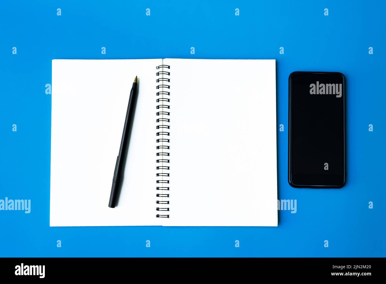 Top view of smart phone, pen and notepad on blue background. Copy space ...