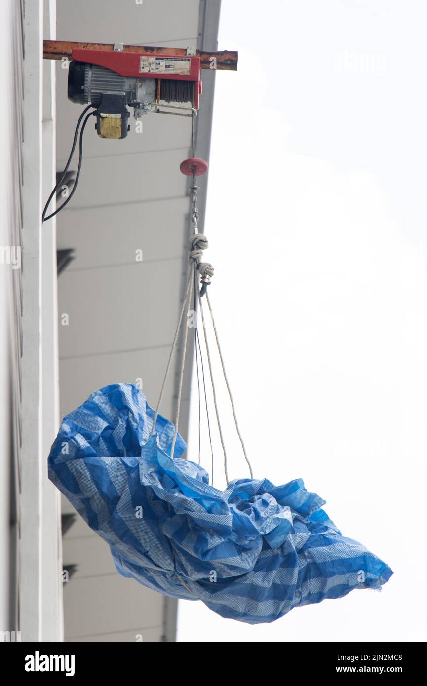 A small electric hoist crane with load is stuck out of a balcony of a ...