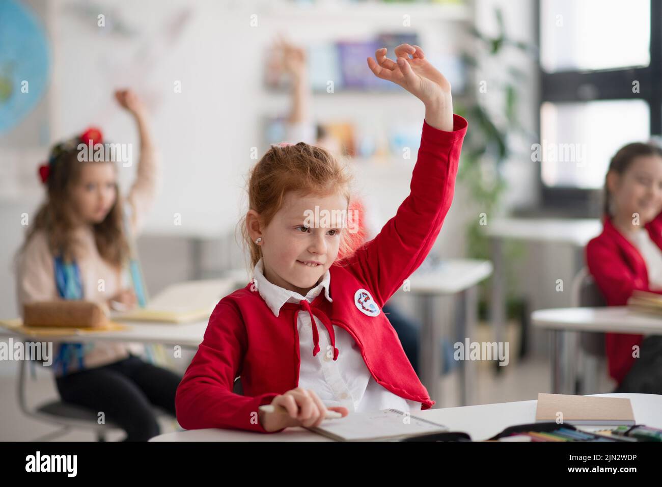 Happy schoolgirl with hands up at lesson in classroom at primary school ...