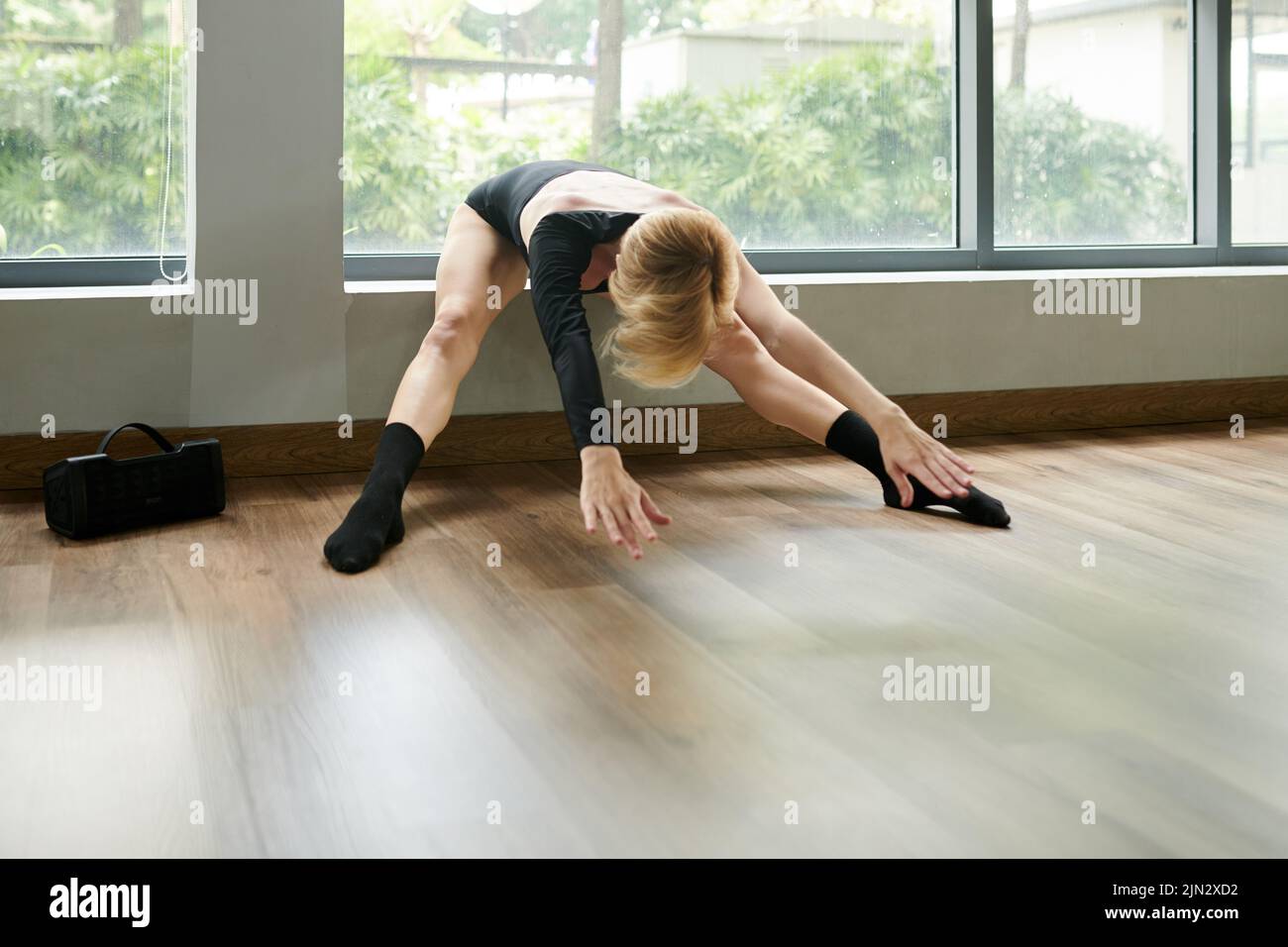 Female dancer bending forward to stretch legs before intense training ...