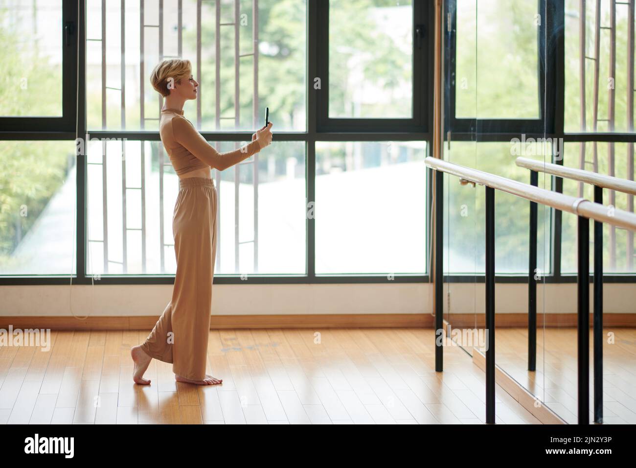 Slim smiling young woman in comfy aparrel taking selfie in dance studio ...
