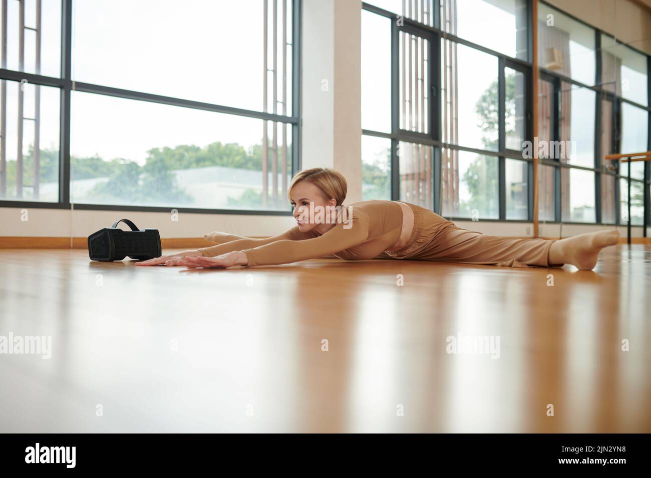 Smiling flexible young woman doing splits and bending forward when ...