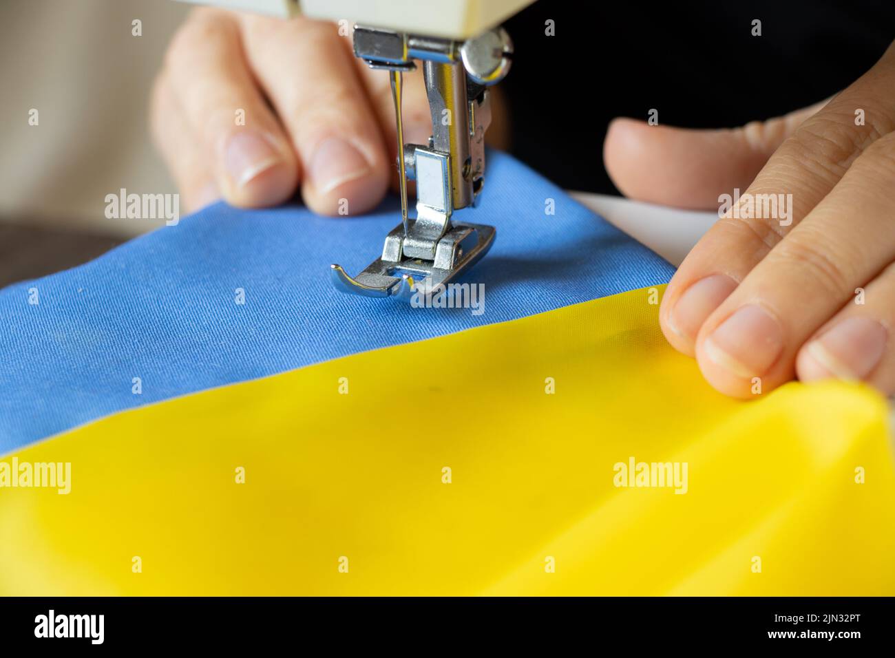A girl sews the flag of Ukraine at home on a sewing machine, the ...