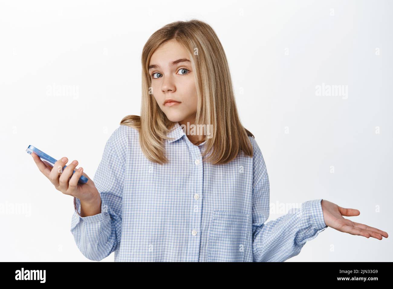 Cute clueless little girl, shrugging while holding mobile phone ...
