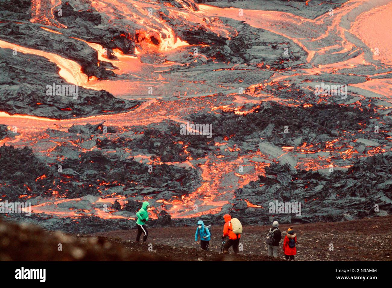 People in special clothes and with backpacks look at the lava flowing ...