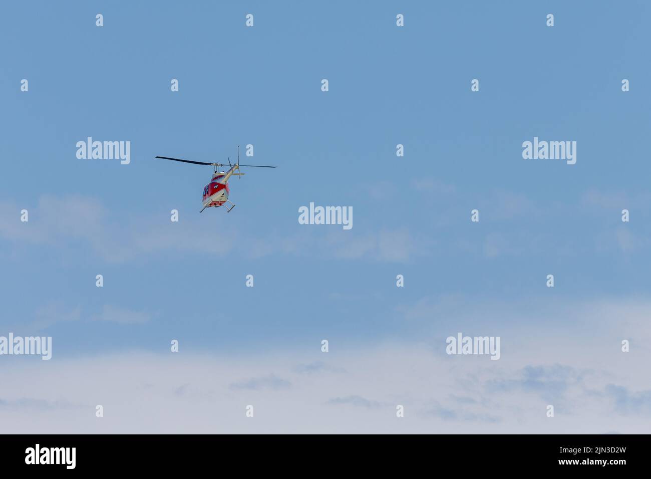 Red helicopter flying into the distant blue sky, above the clouds, and ...