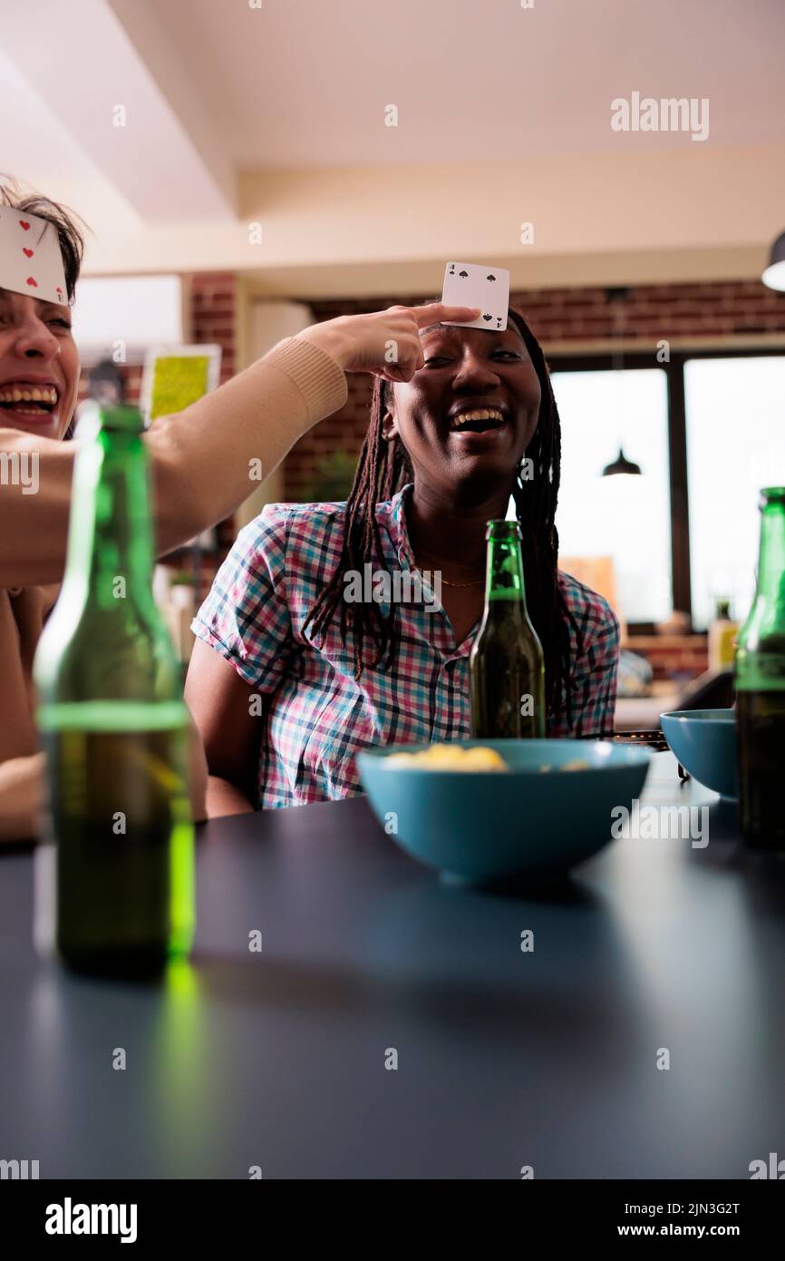 Cheerful multiethnic women playing card guessing game with friends in ...