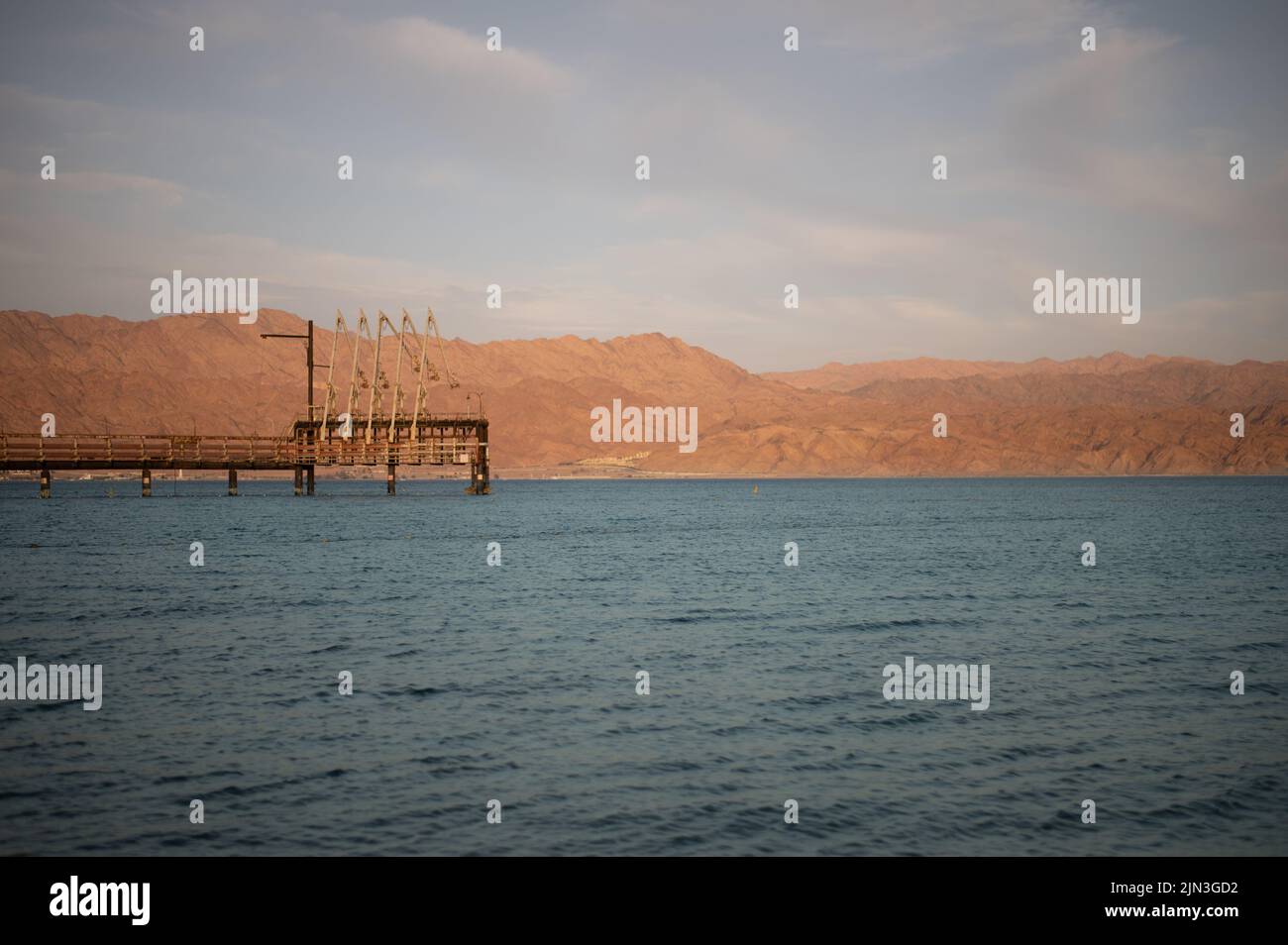 A pier on the sea with rocky cliff in the background under cloudy sky ...