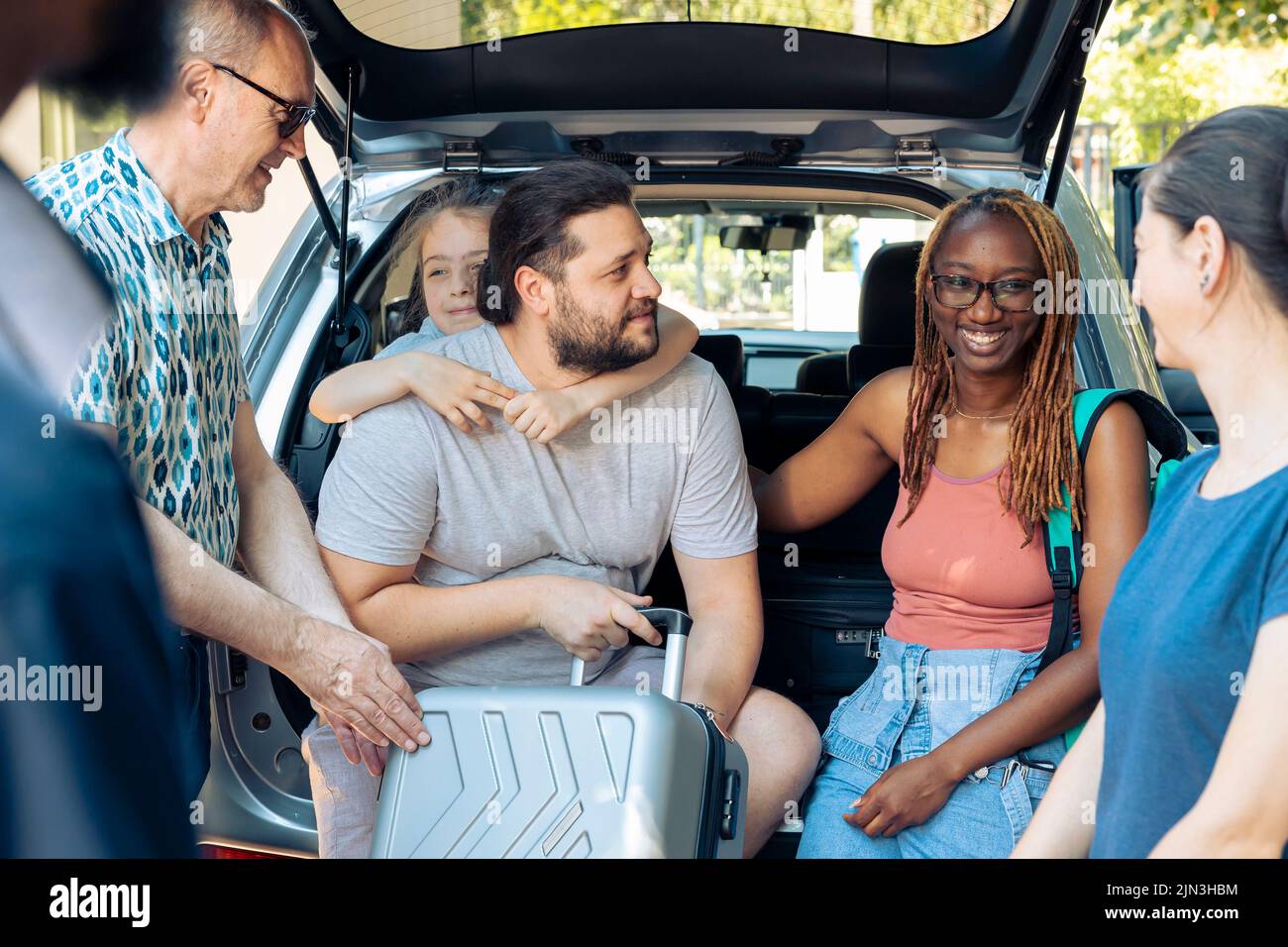 Diverse family and friends loading trolley in automobile trunk ...
