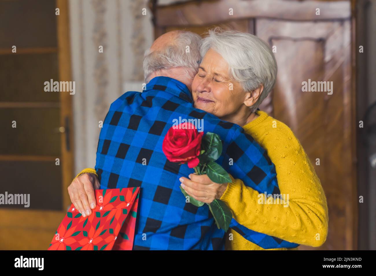 Happy womens day. Caring and loving caucasian elderly husband surprising his wife with a red ...