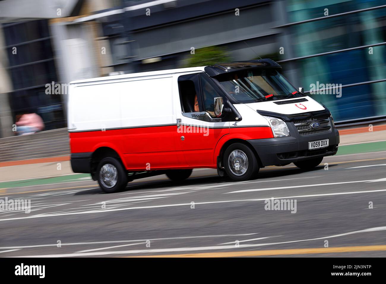A panning shot of a Red & White Ford transit van travelling through ...