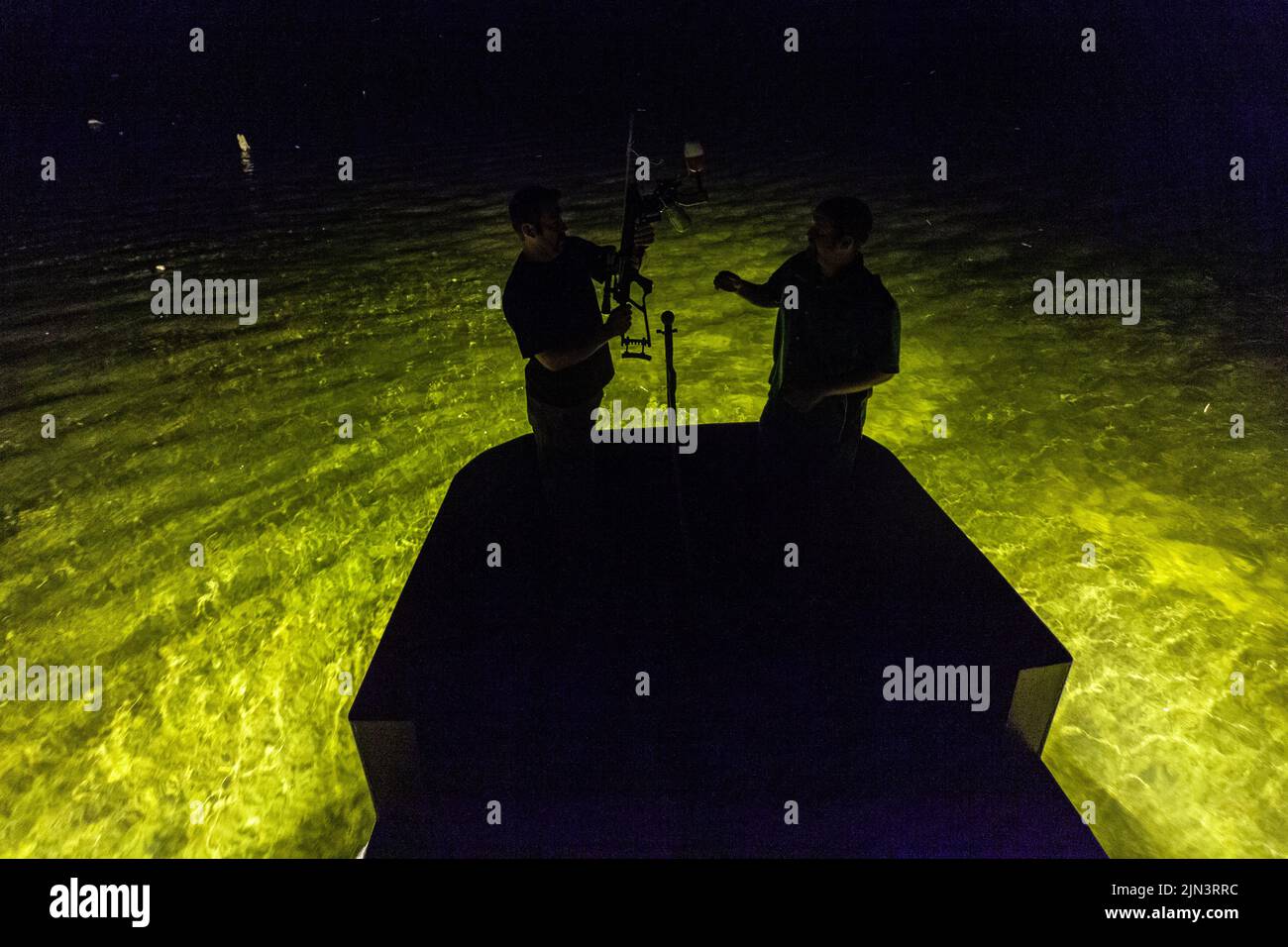 An alligator hunting guide and his client are silhouetted by underwater ...