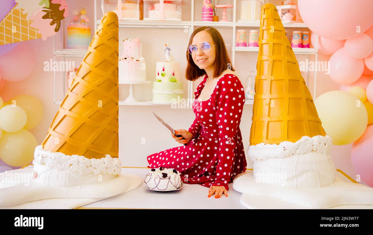 Young woman in red dress sitting on table, cutting cake with knife in ...