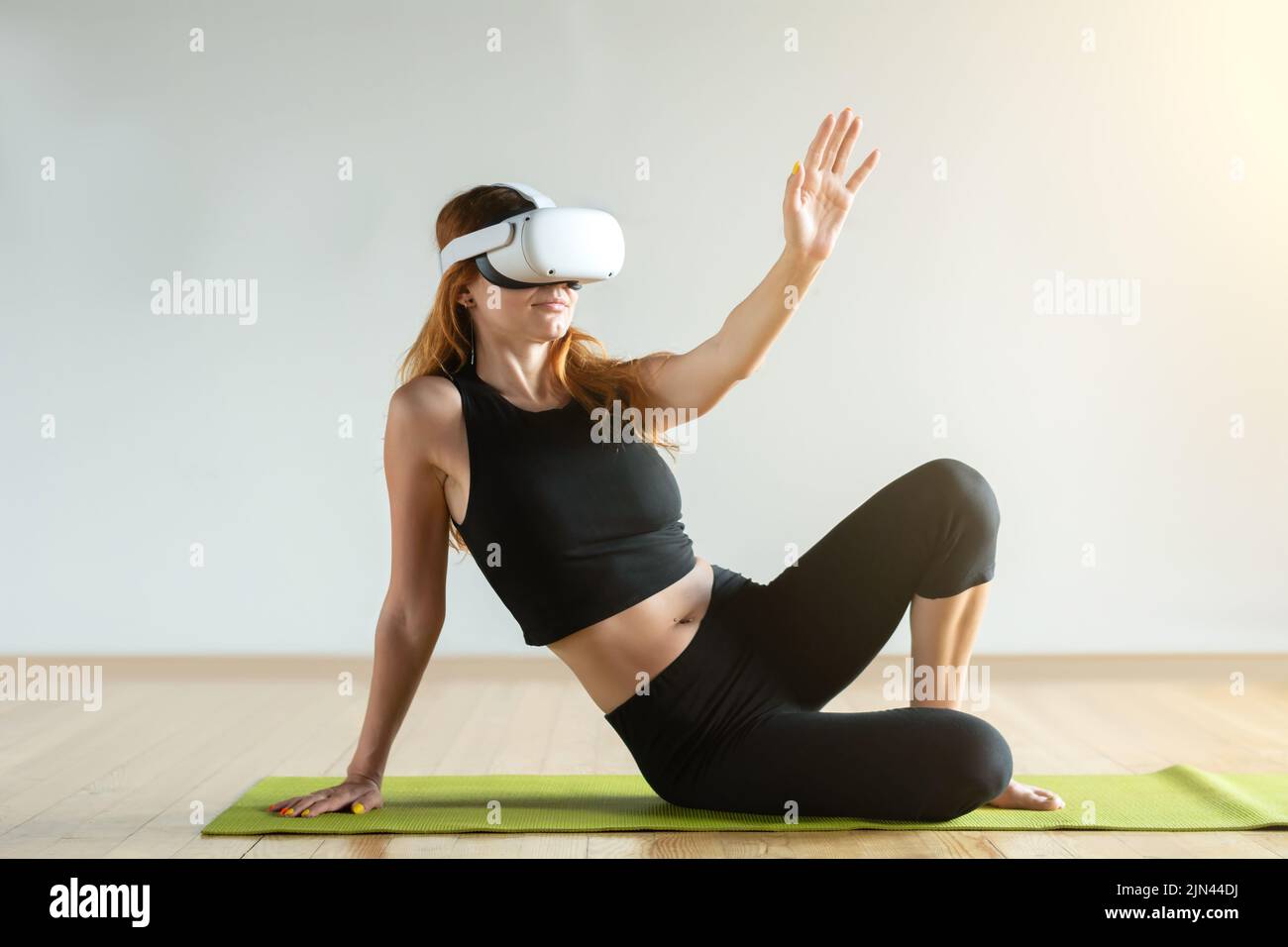 A young woman in virtual reality glasses makes fitness exercises ...