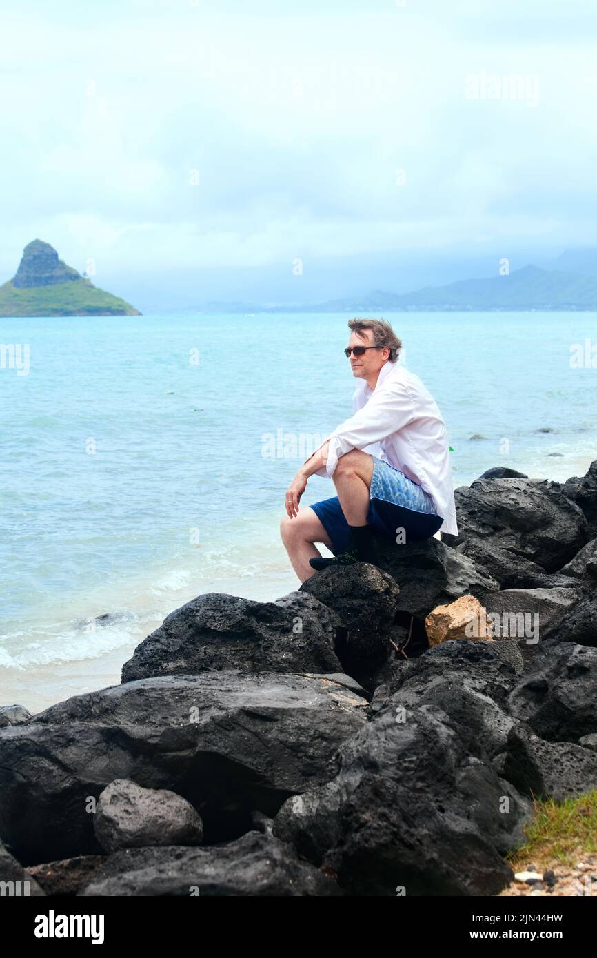 Handsome Caucasian man in forties sitting on rocky shore of hawaiian ...