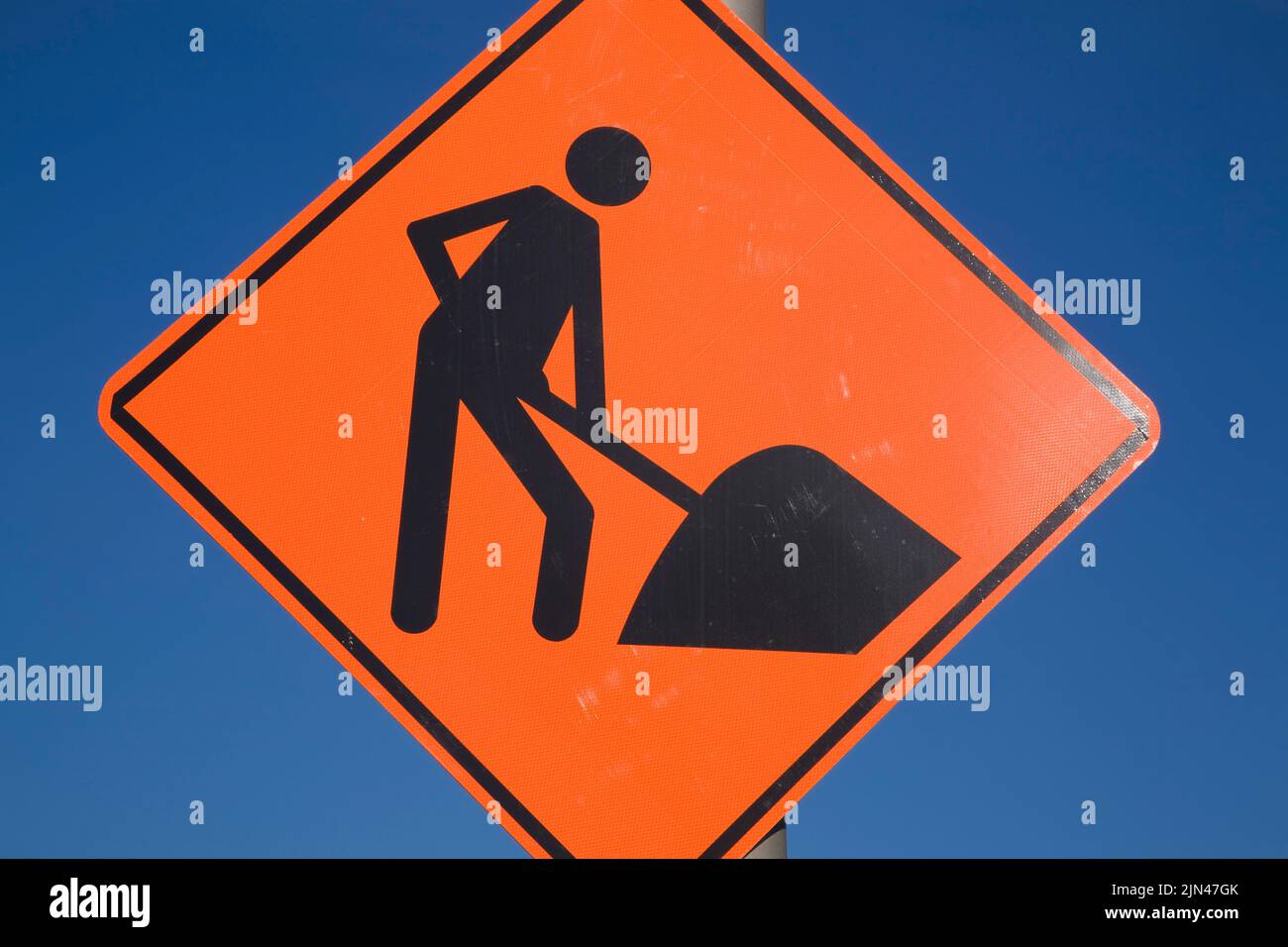 Orange pictogram Men at Work warning sign on metal pole against a blue ...