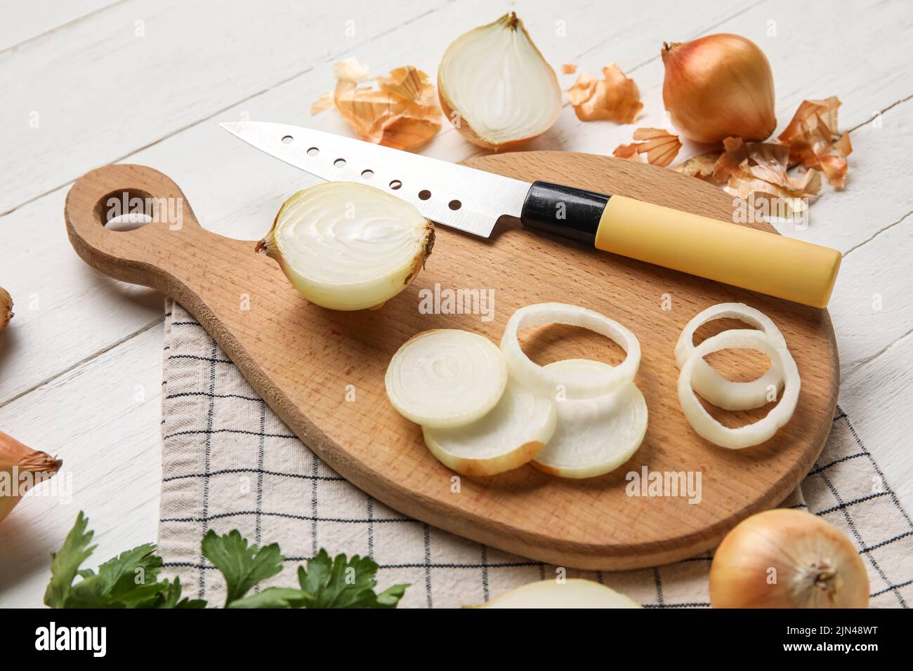 Board with cut onion and knife on light wooden background, closeup ...