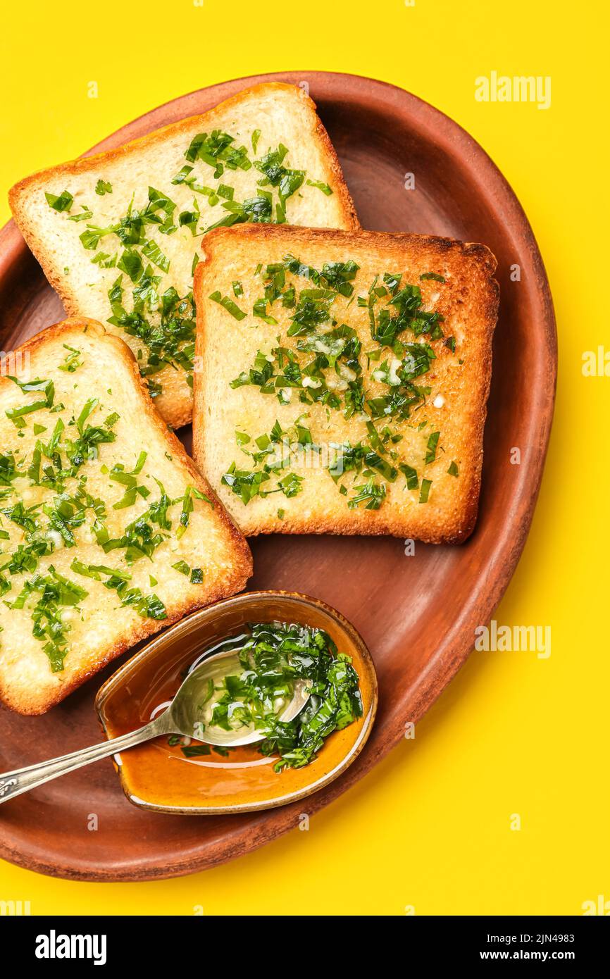 Plate of toasts with garlic, parsley and oil on yellow background ...