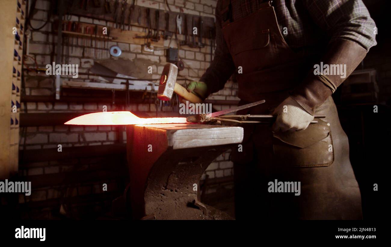 A man blacksmith forging a hot knife blade using a hammer Stock Photo ...
