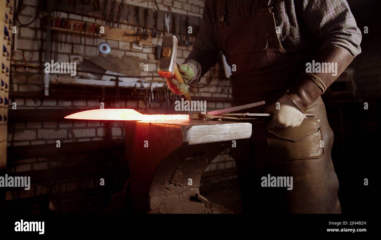 A man blacksmith forging a knife blade using a hammer Stock Photo - Alamy
